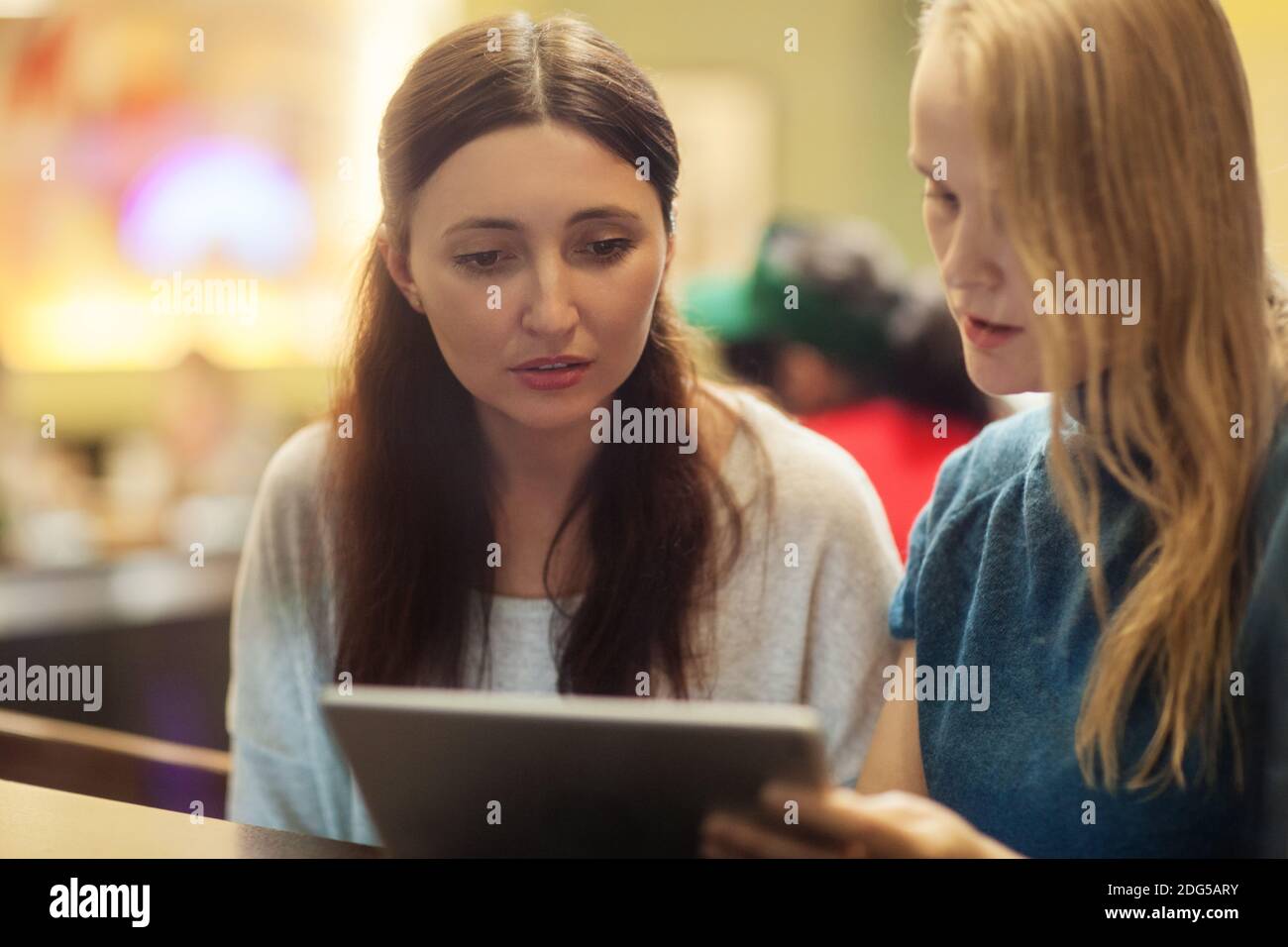 Two women have a discussion in the restaurant using electronic tablet ...