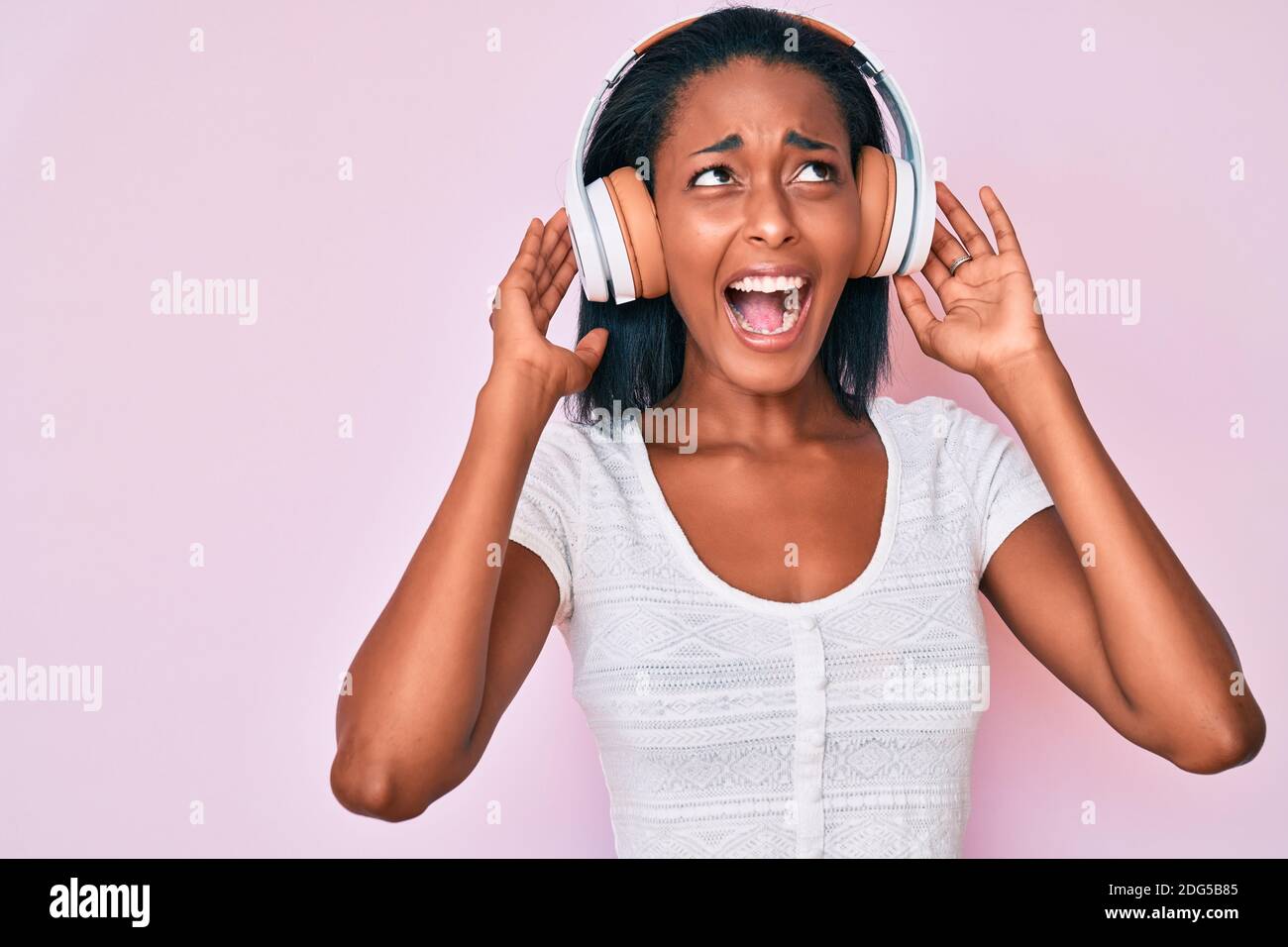 Young african american woman listening to music using headphones angry ...