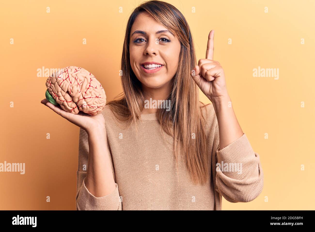 Young beautiful woman holding brain smiling with an idea or question ...