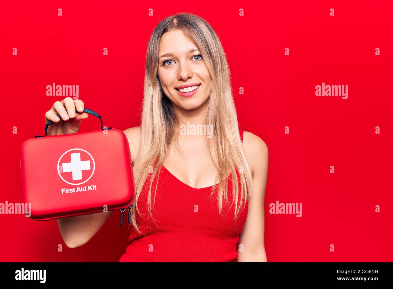 Young blonde woman holding first aid kit looking positive and happy ...