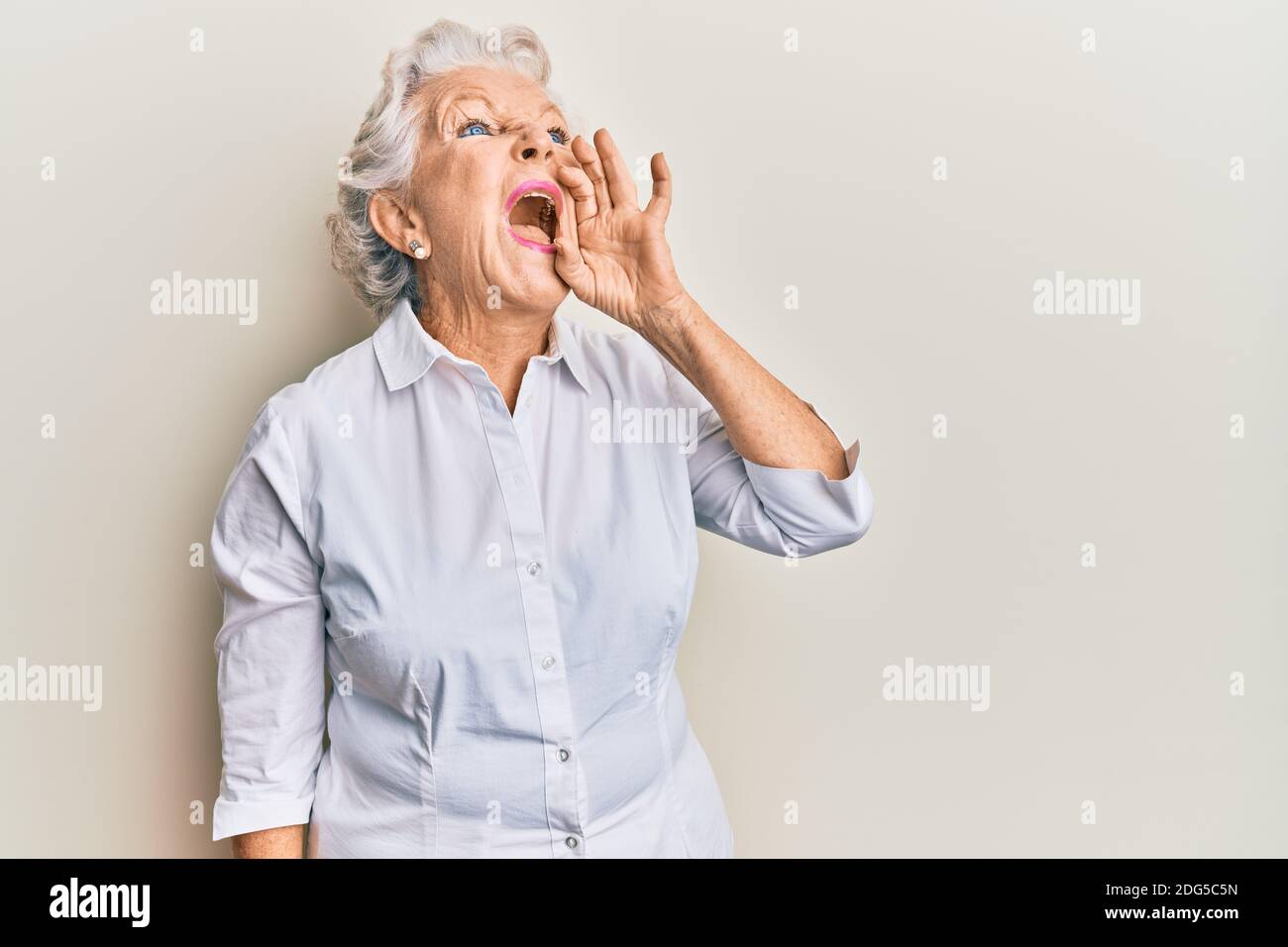 Senior grey-haired woman wearing casual clothes shouting and screaming ...
