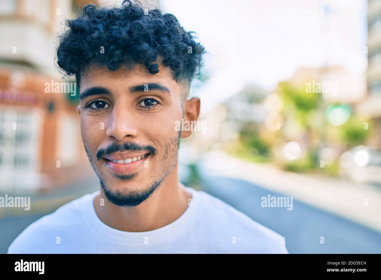 Young arab man smiling happy looking to the camera at street of city ...