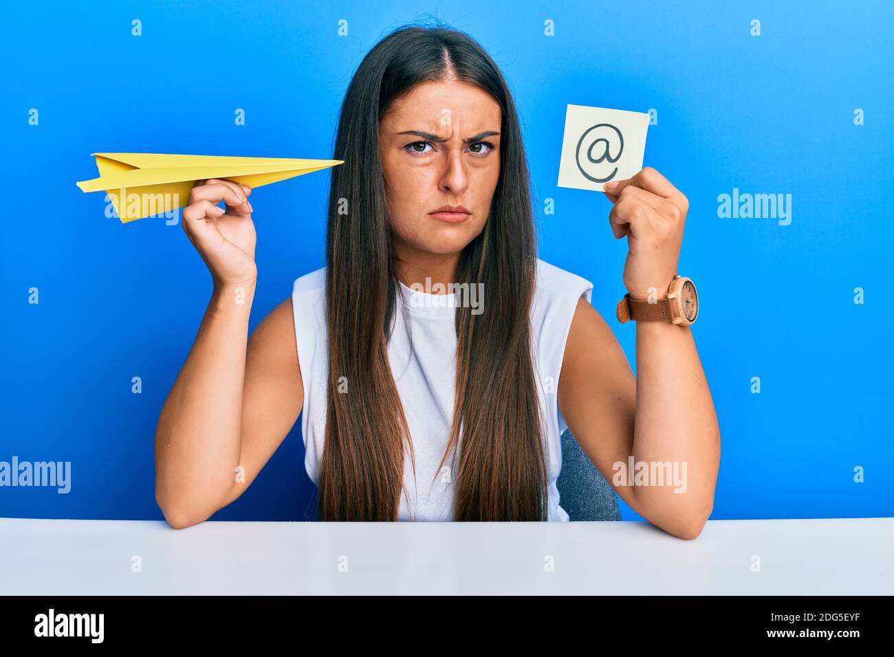 Beautiful hispanic woman holding paper plane and email symbol clueless ...