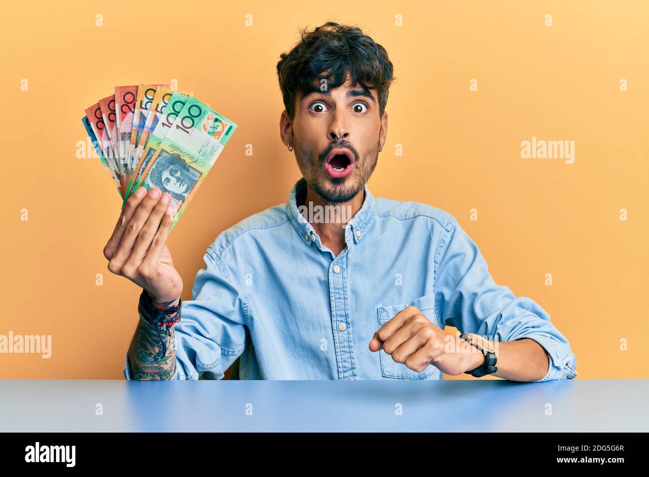 Young hispanic man holding australian dollars sitting on the table ...