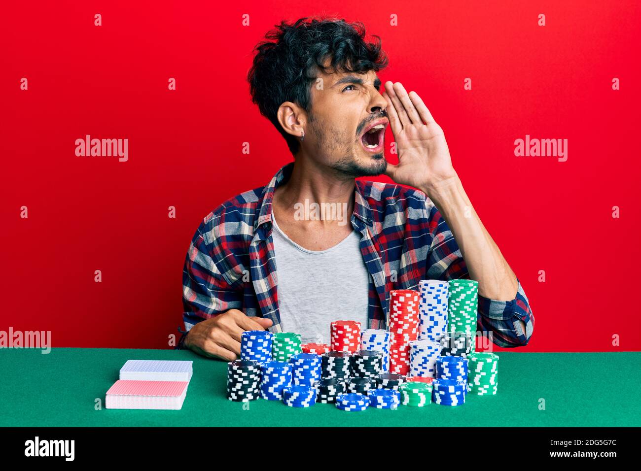 Young hispanic man sitting on the table with poker chips and cards ...