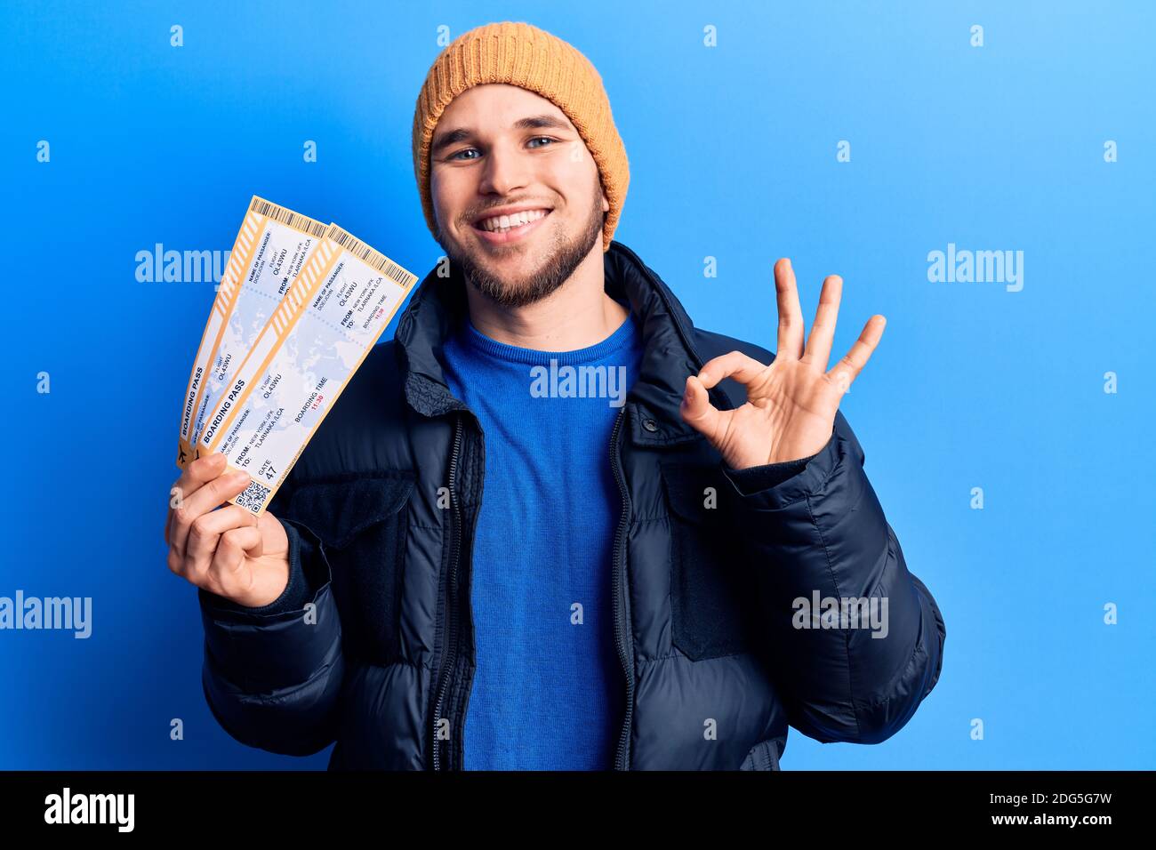 Young handsome man wearing winter clothes holding airline boarding pass ...