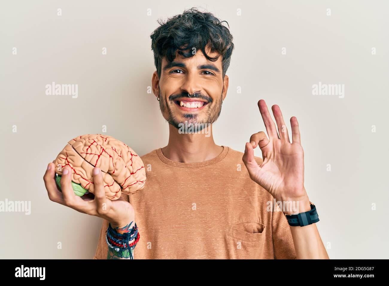 Young hispanic man holding brain doing ok sign with fingers, smiling ...