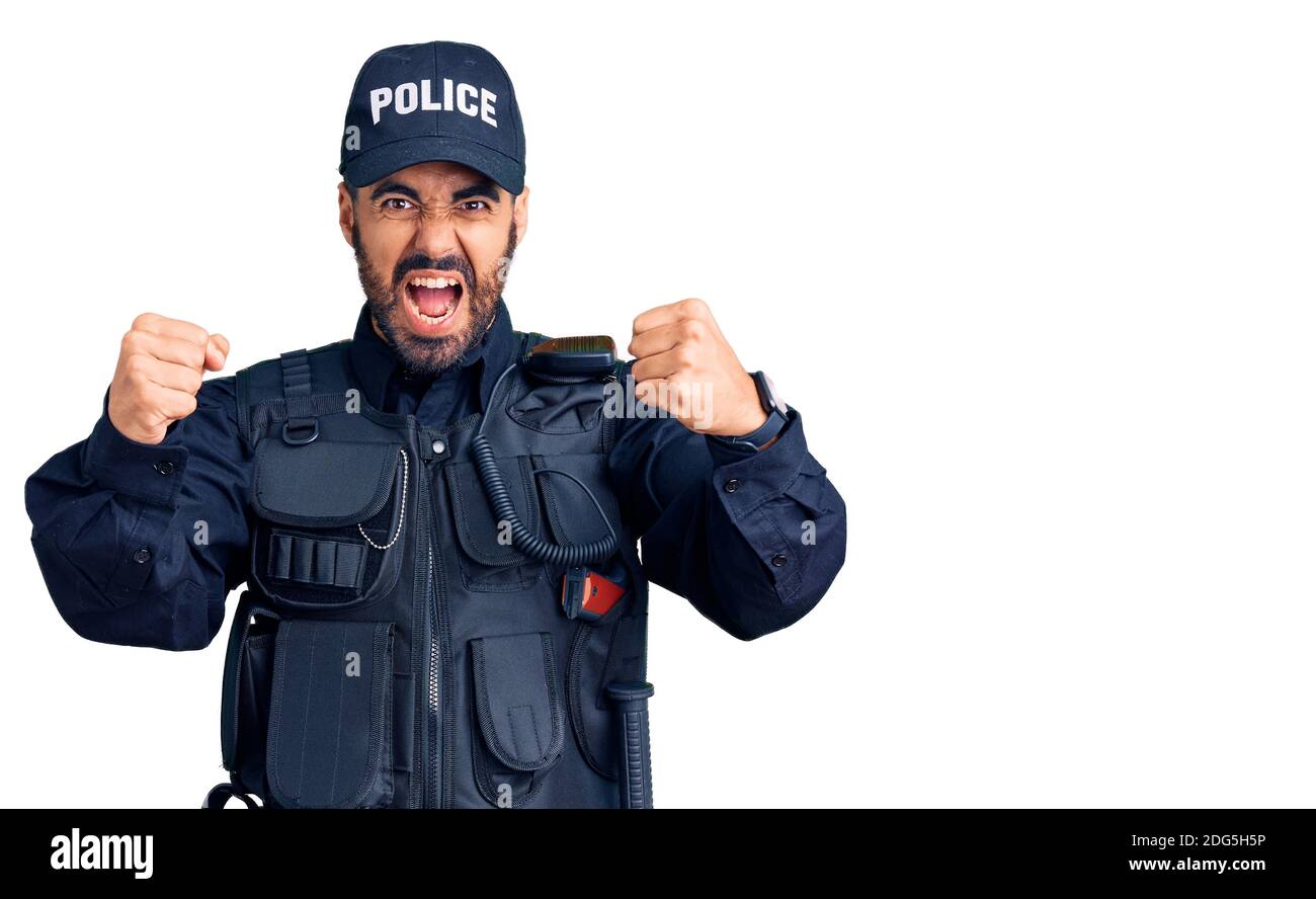 Young hispanic man wearing police uniform angry and mad raising fists ...