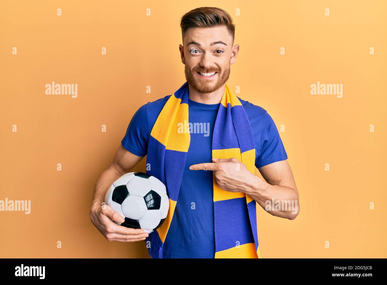 Young redhead man football hooligan holding ball smiling happy pointing ...