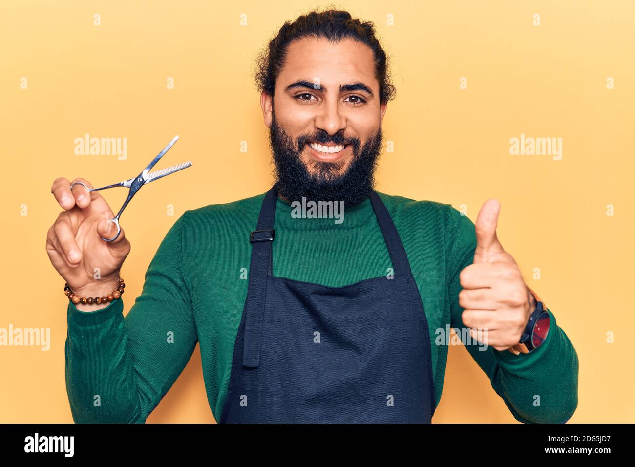 Young arab man wearing barber apron smiling happy and positive, thumb ...