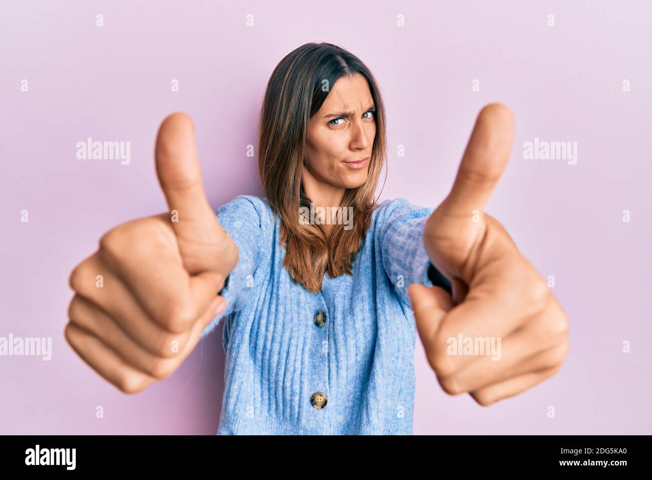 Brunette young woman doing thumbs up positive gesture in shock face ...