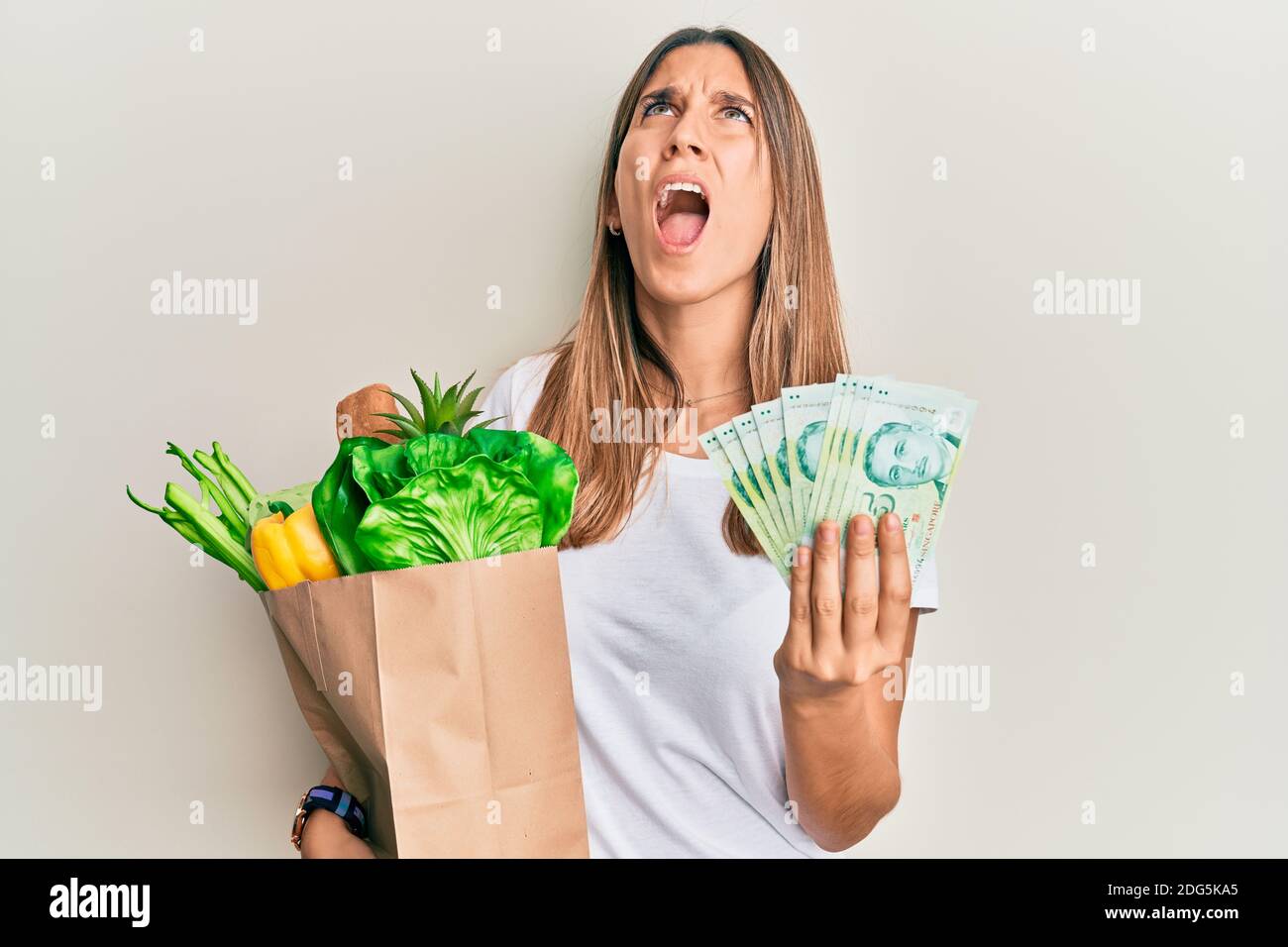 Brunette young woman holding groceries and singapore dollars banknotes ...