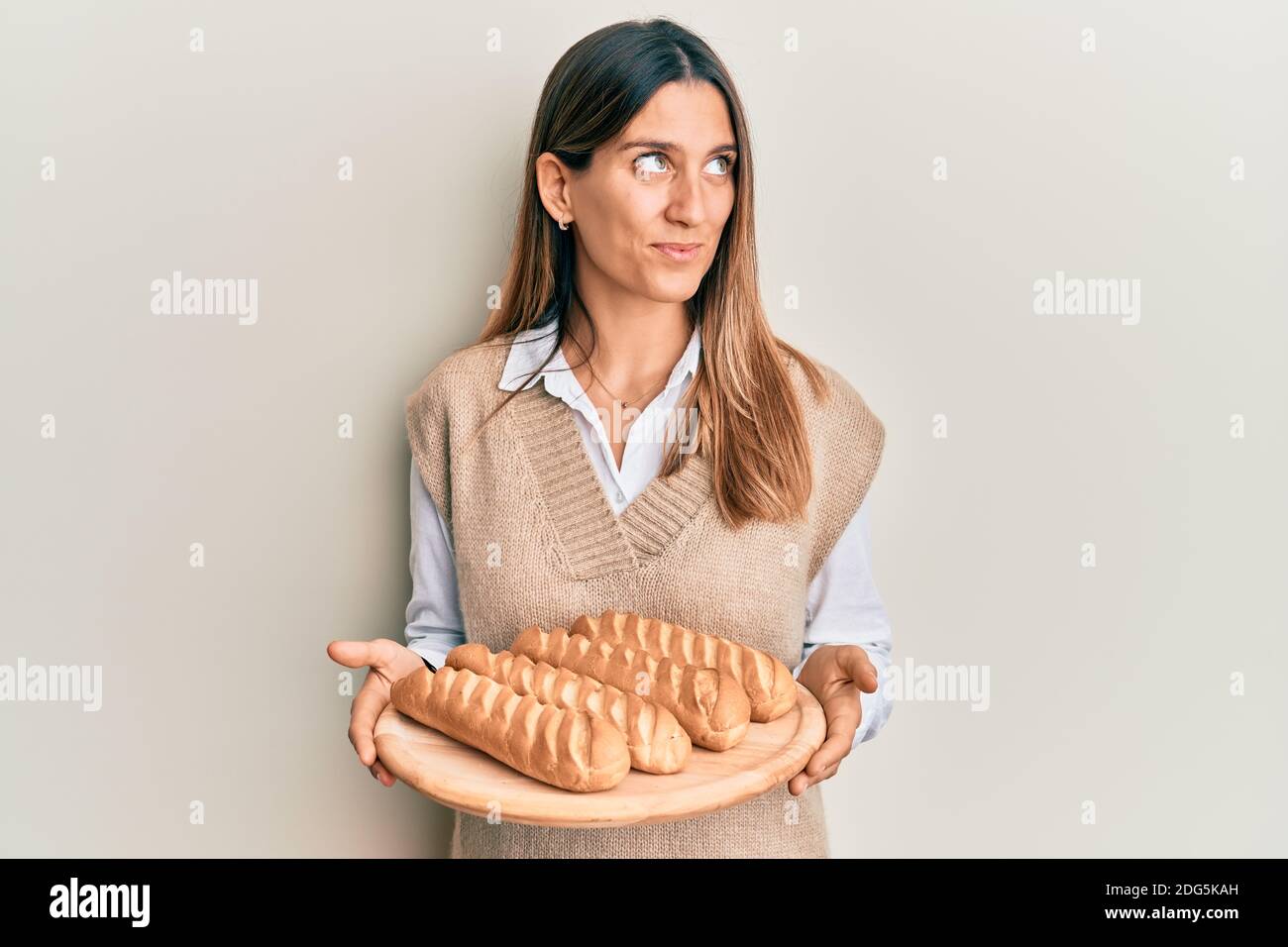 Brunette young woman holding homemade bread smiling looking to the side ...