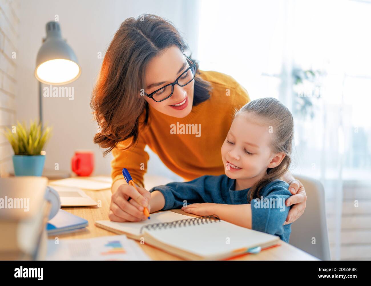 Happy child and adult are sitting at desk. Girl doing homework or ...