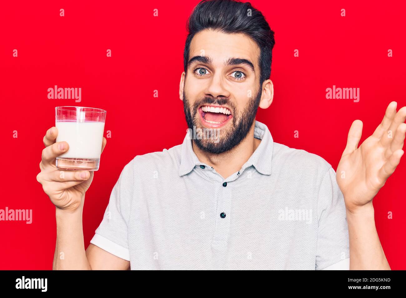 Young handsome man with beard drinking glass of milk celebrating ...