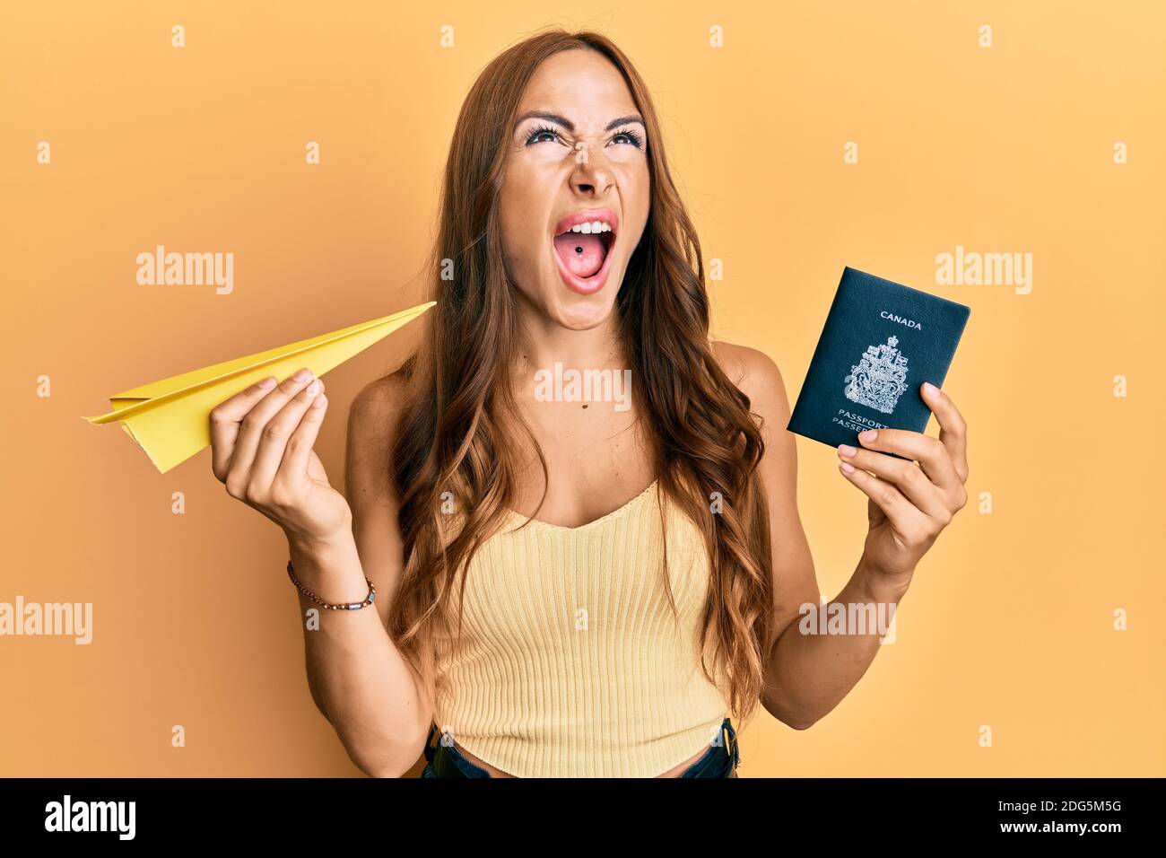 Young brunette woman holding paper airplane and canadian passport angry ...