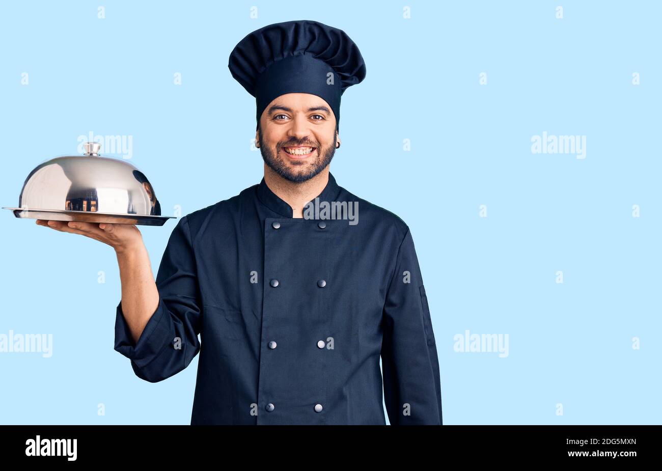 Young hispanic man wearing cooker uniform holding tray looking positive ...