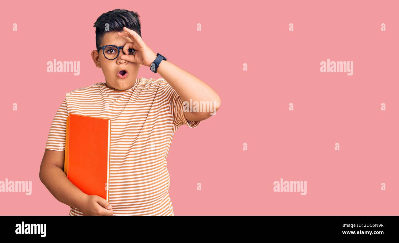 Little boy kid holding book wearing glasses doing ok gesture shocked ...