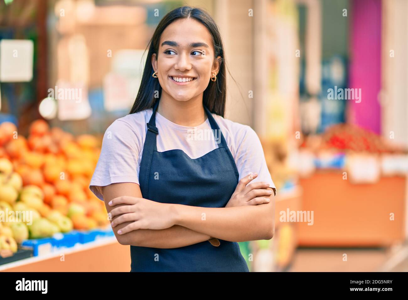 Young latin shopkeeper girl with arms crossed smiling happy at the ...