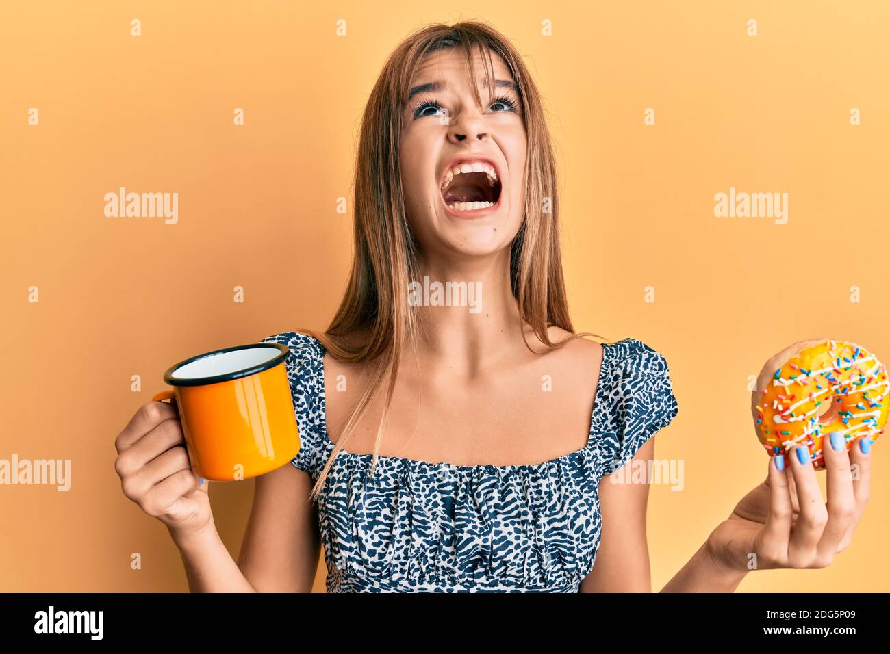 Teenager caucasian girl eating doughnut and drinking coffee angry and ...