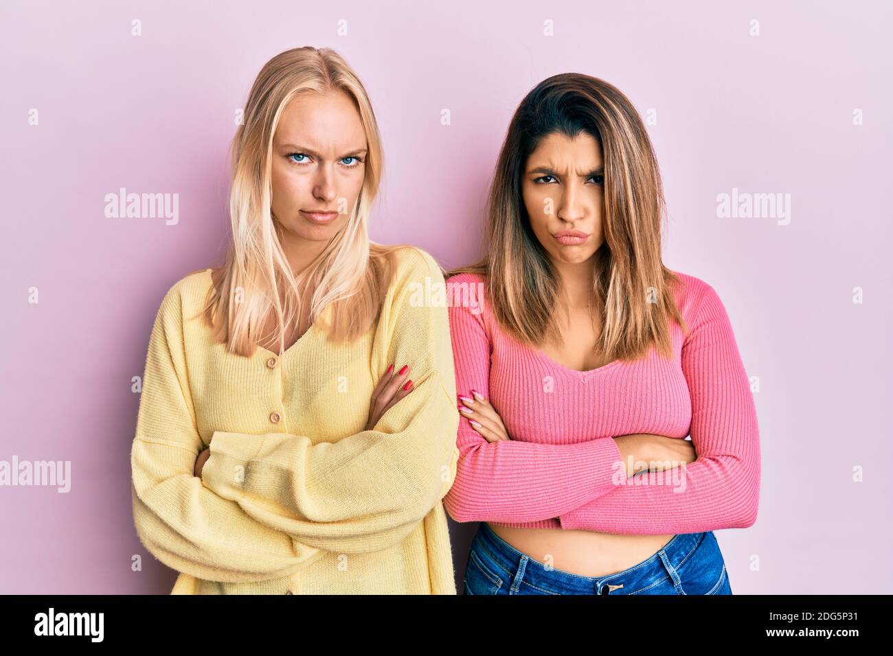 Two friends standing together over pink background skeptic and nervous ...