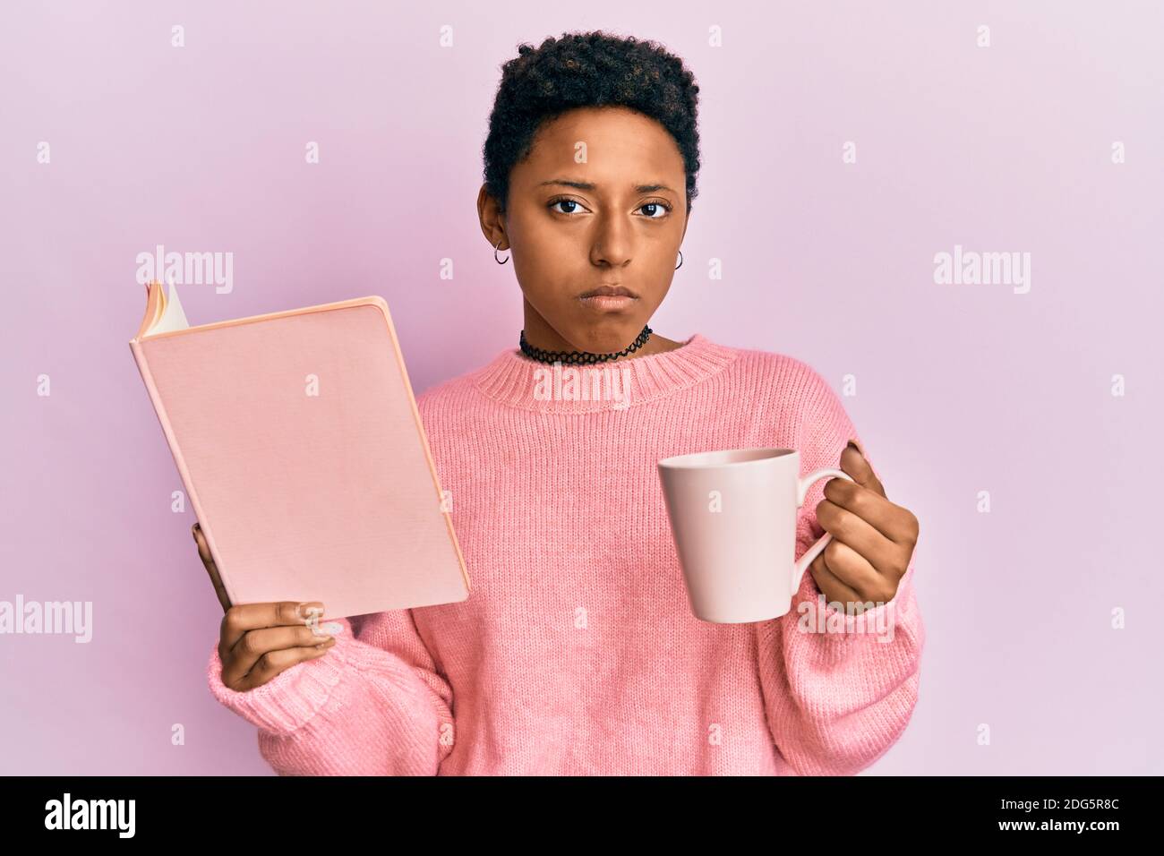Young african american girl reading a book and drinking a cup of coffee ...