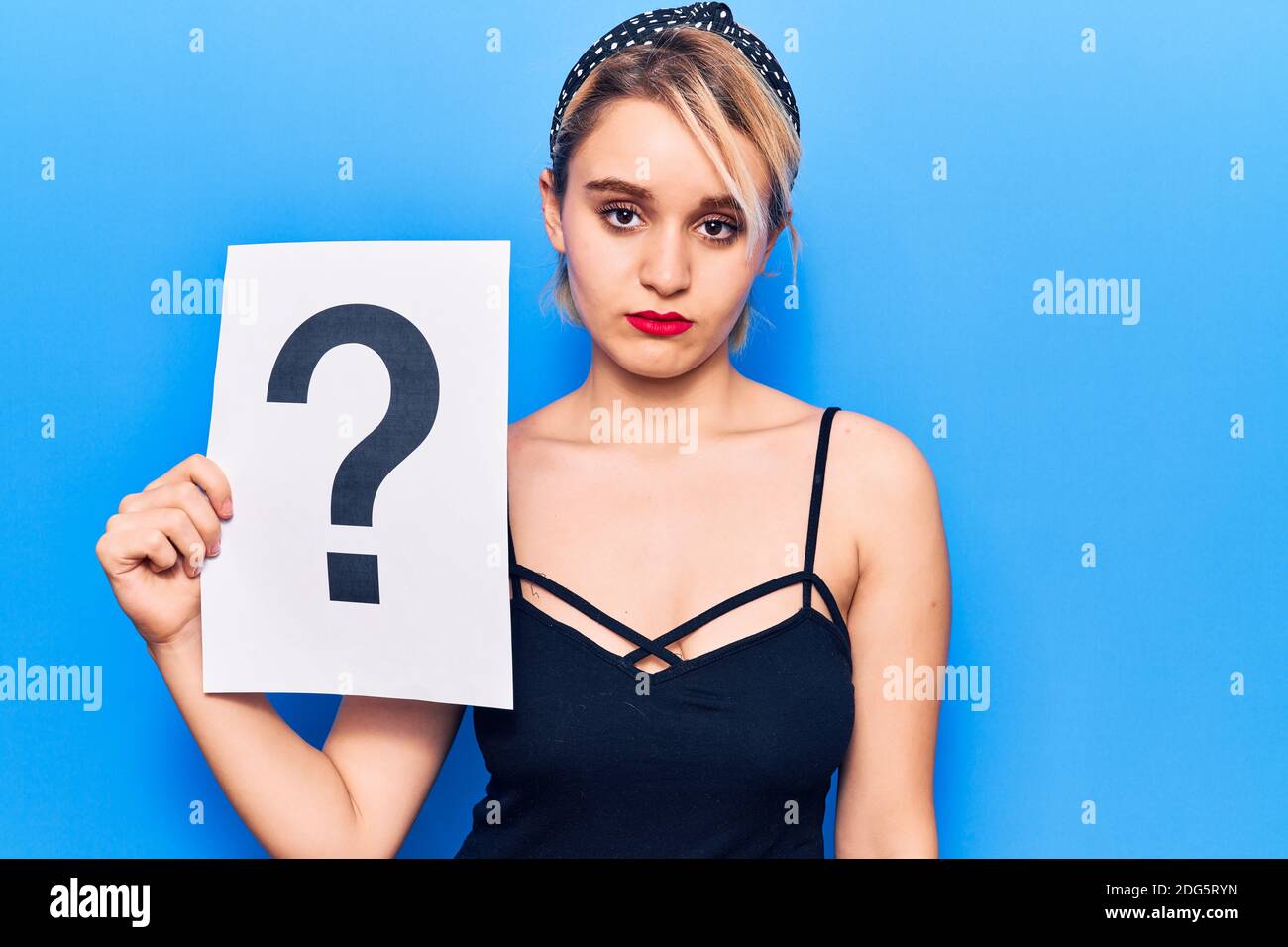 Young beautiful blonde woman holding question mark thinking attitude ...