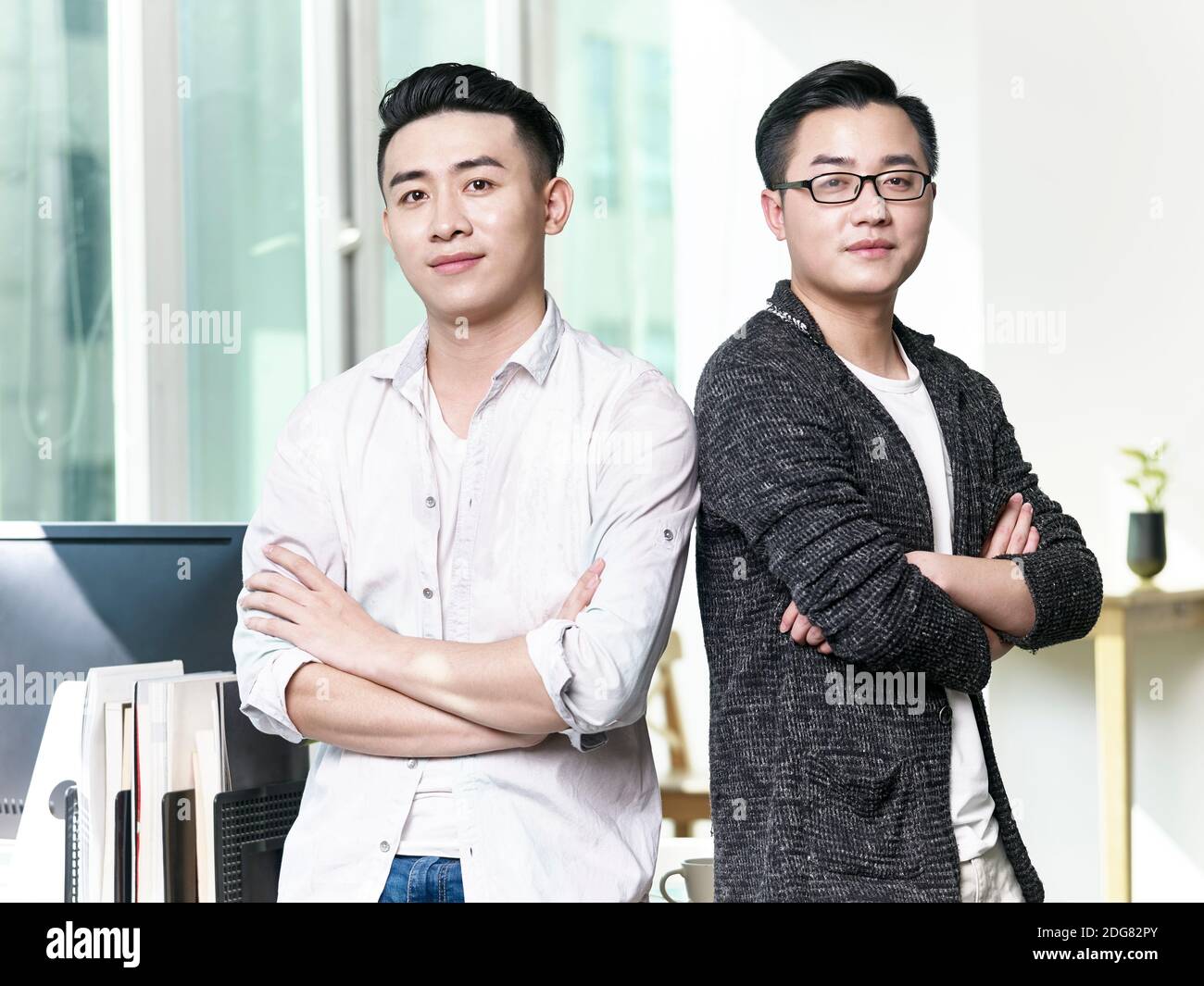 portrait of two young asian entrepreneurs standing back to back in ...