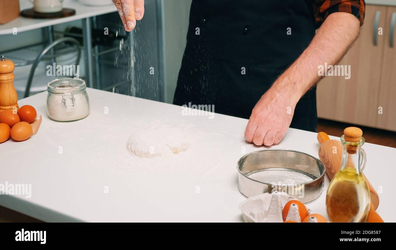 Hands of chef man sifting flour on dough for baking. Elderly senior ...