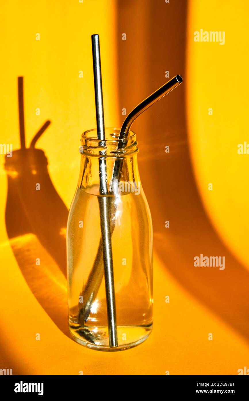 Reusable Metal Straws in glass bottle with water on yellow background ...
