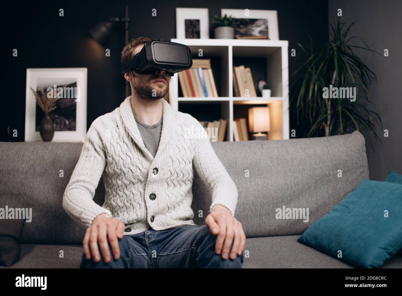 Young guy in casual clothing using modern VR headset during leisure ...