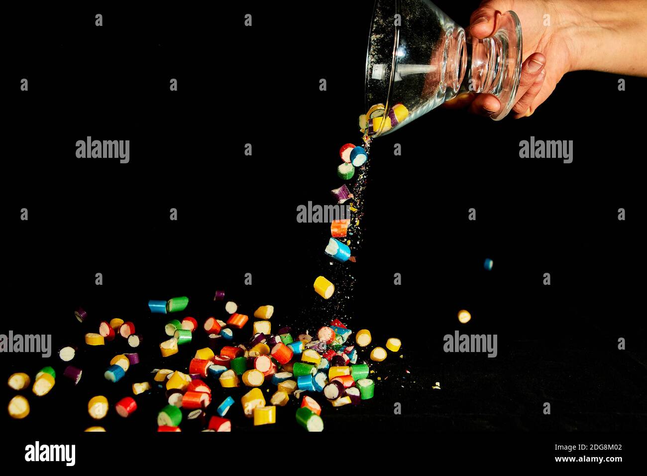 sugar candies falling from glass container on black table background ...