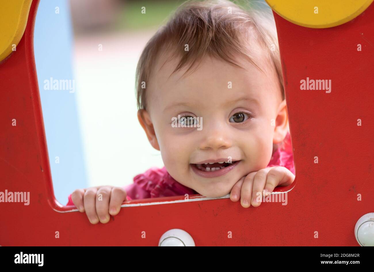 Cute baby girl having fun on a playground and looking at the camera ...