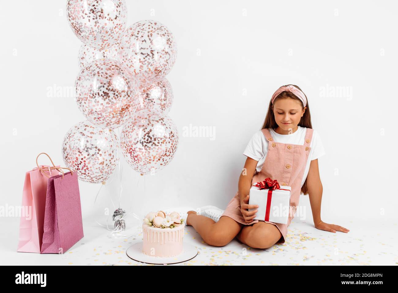 Happy young girl, with balloons, big beautiful cake and gift, sitting ...