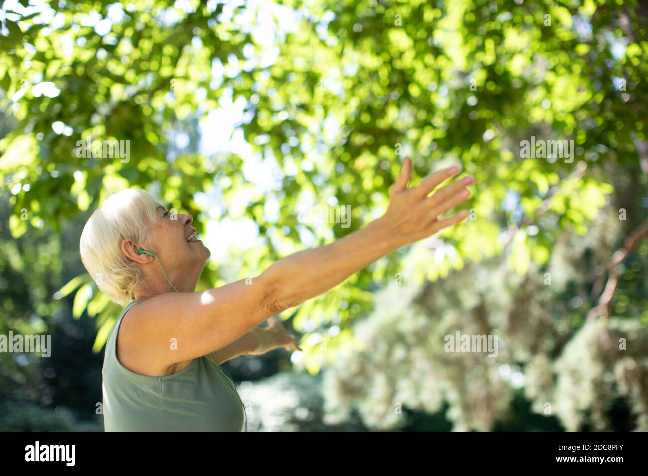 Carefree senior woman with arms outstretched under summer trees Stock ...