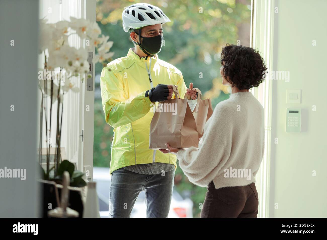 Woman receiving food delivery from man in face mask and helmet Stock ...