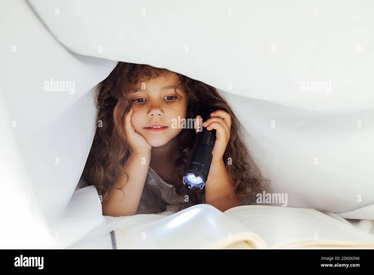 girl reads a book with a flashlight under a blanket in bed Stock Photo ...