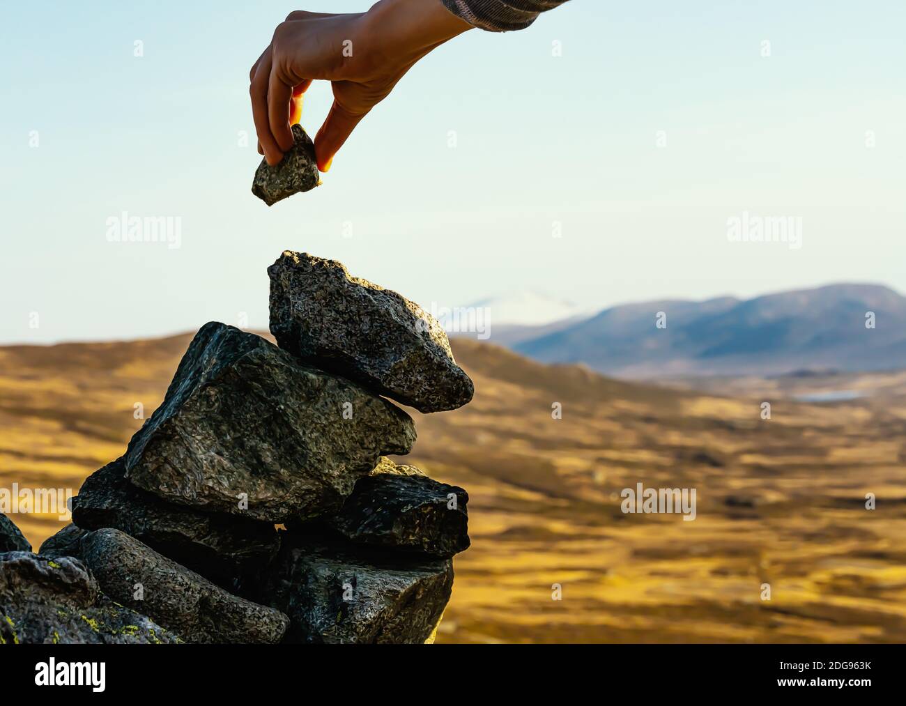 Hand placing a rock on top of a cairn on the peak of a mountain. Close ...