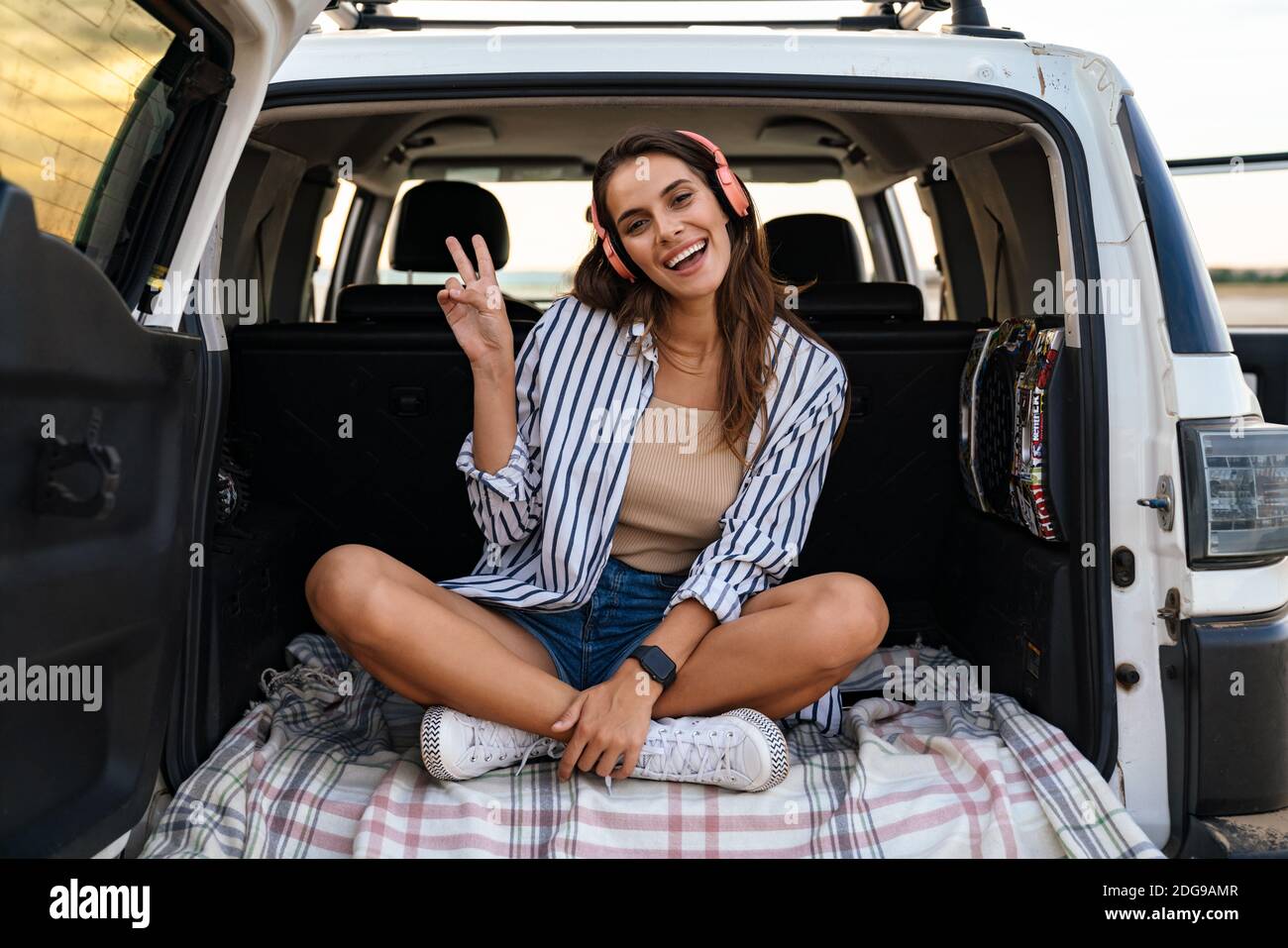 Young smiling young woman with headphones sitting in back of a car ...