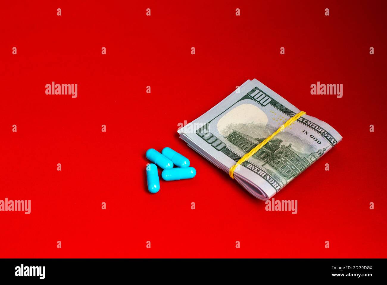 Bundle of money and blue pharmaceutical pills, medicines on a red ...