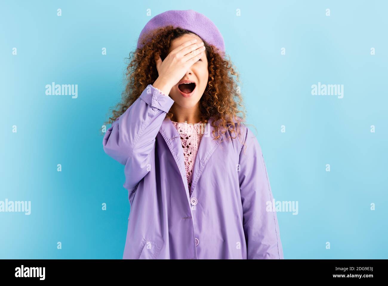 scared and curly woman in beret covering face with hands and screaming ...