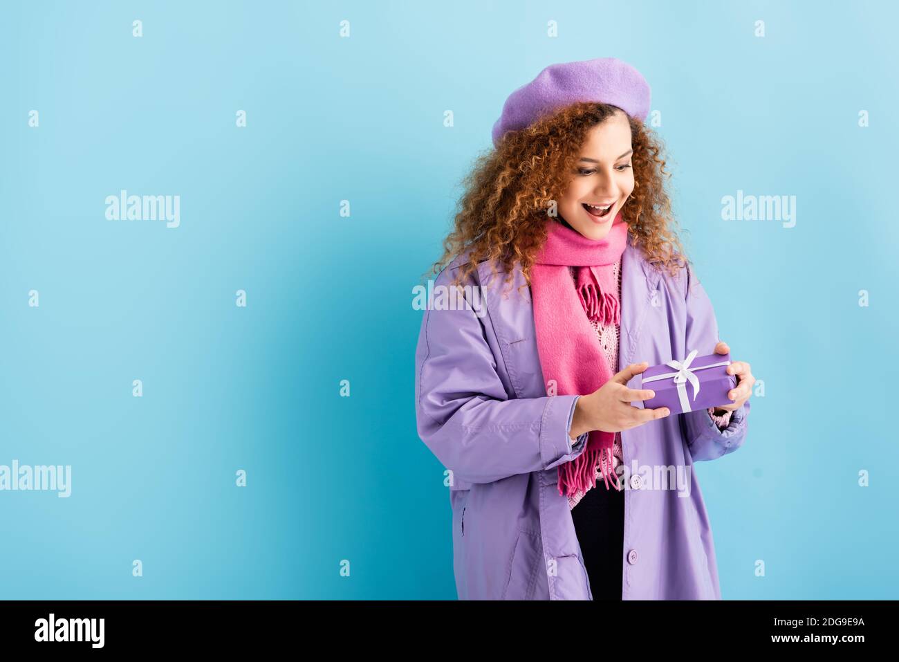 young amazed woman in winter coat, beret and pink knitted scarf holding ...