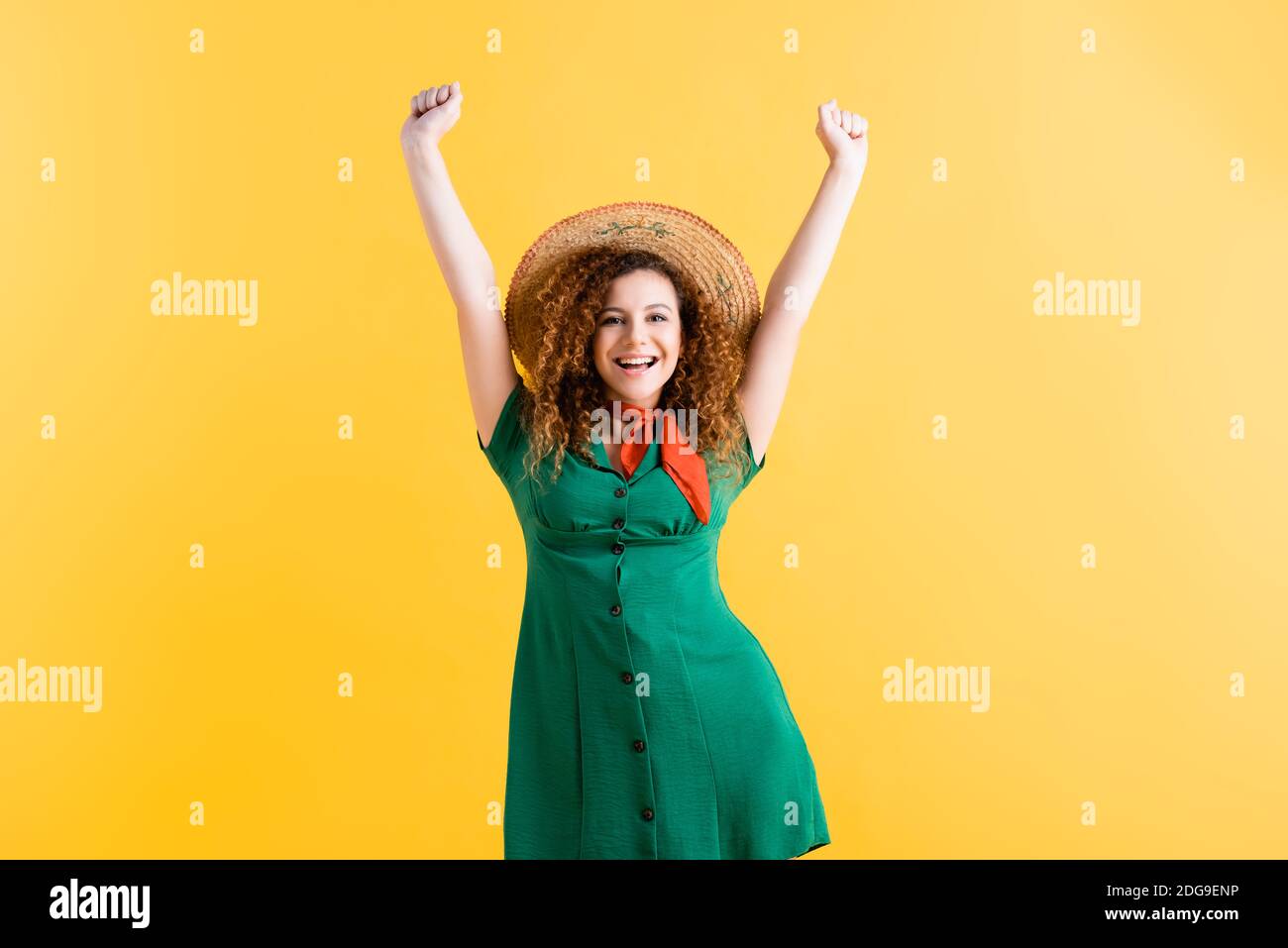 amazed woman in green dress and straw hat standing with hands above ...