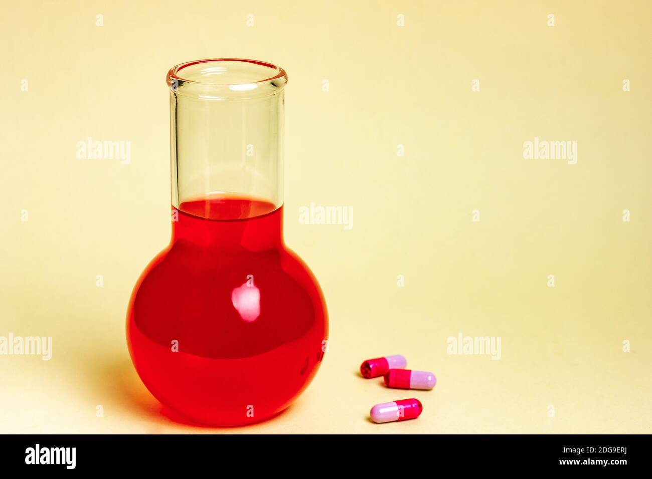 Chemical flask with red liquid and pharmaceutical pills on yellow ...