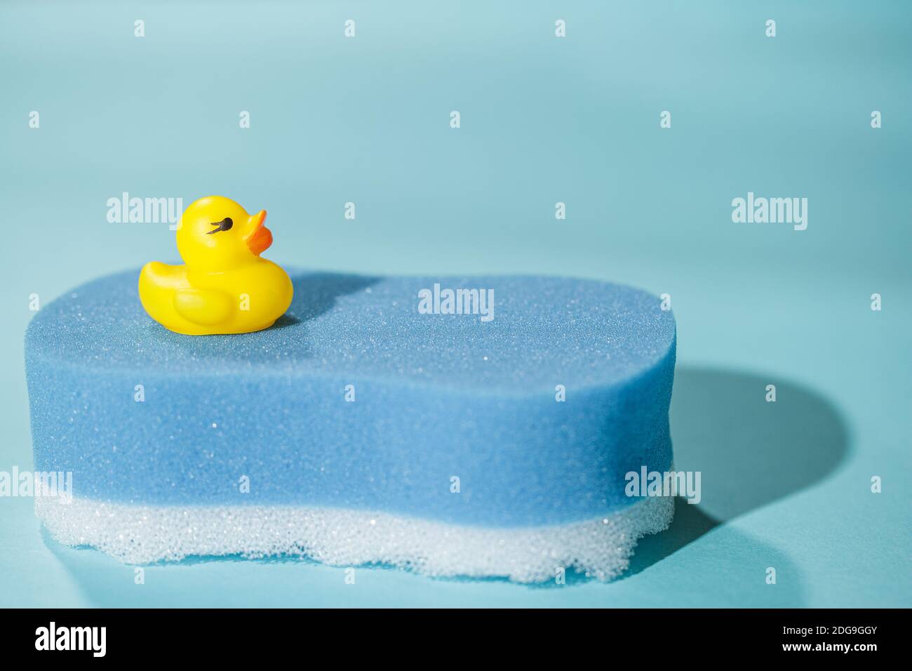 Small yellow rubber duck on blue bath sponge, on blue background ...