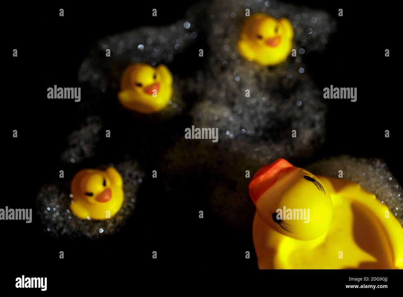 Top view of yellow rubber ducks with foam on a black background with ...