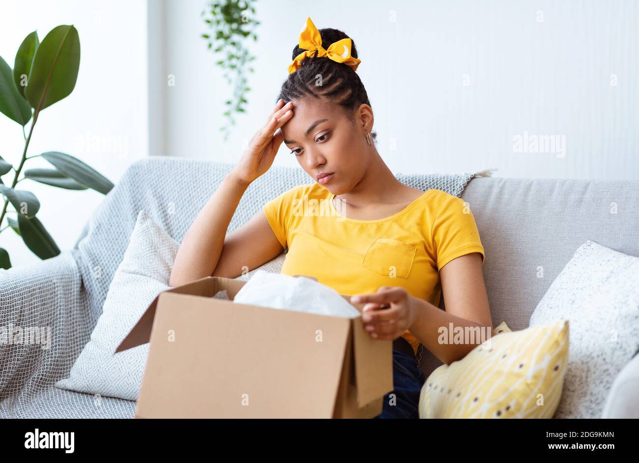 Sad young lady unpacking wrong parcel, delivery mistake Stock Photo - Alamy