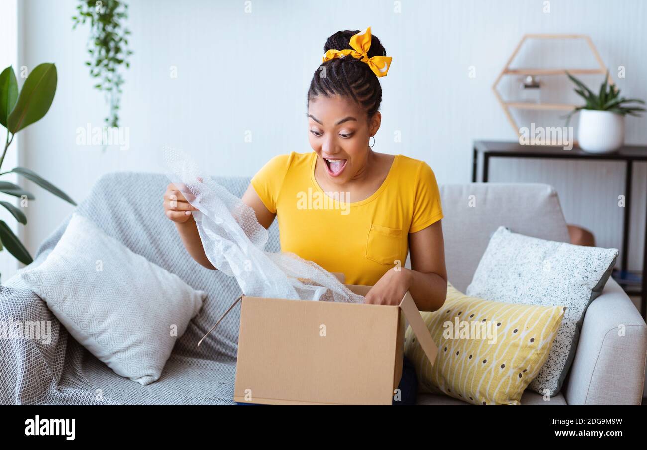 Excited black woman unpacking box after online shopping Stock Photo - Alamy