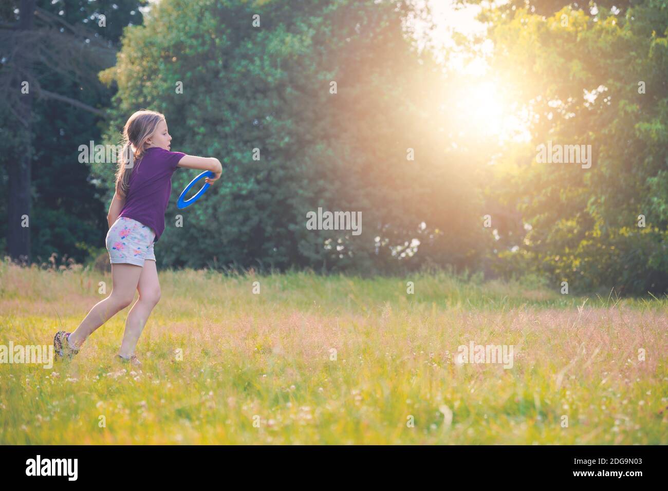 Little girl throwing Frisbee in the park in summer on a sunny warm day ...