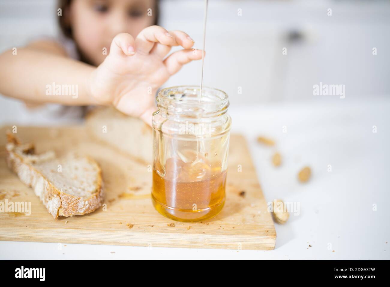 Little girl picking honey from a jar next to a slice of bread Stock ...